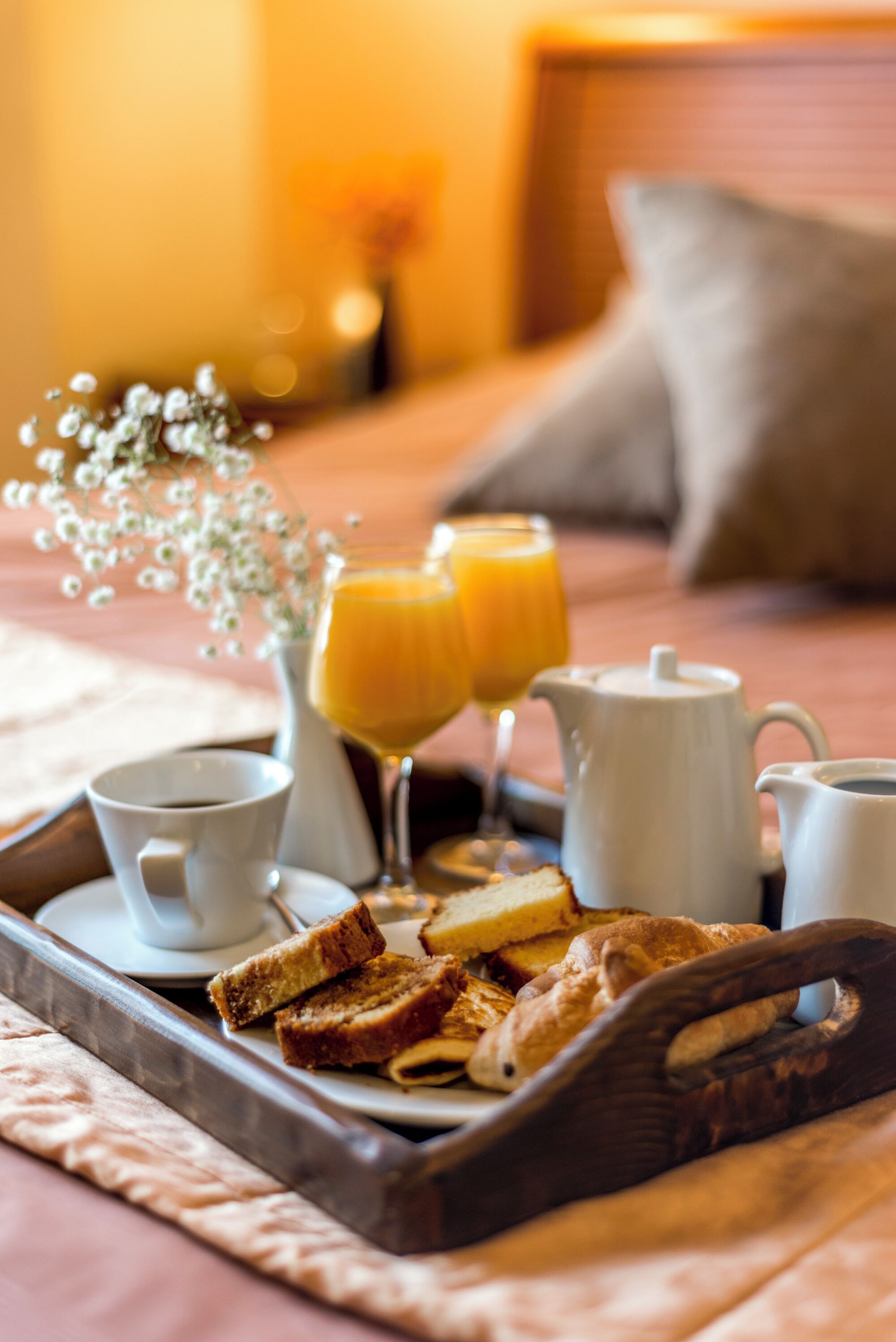 Bandeja de café da manhã com torradas, uma xícara de café, um copo de suco de laranja e uma chaleira na cama.