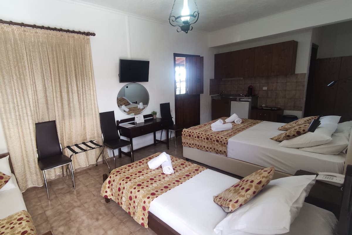 Quarto de hotel com duas camas, uma escrivaninha, uma cadeira, televisão e uma pequena cozinha.