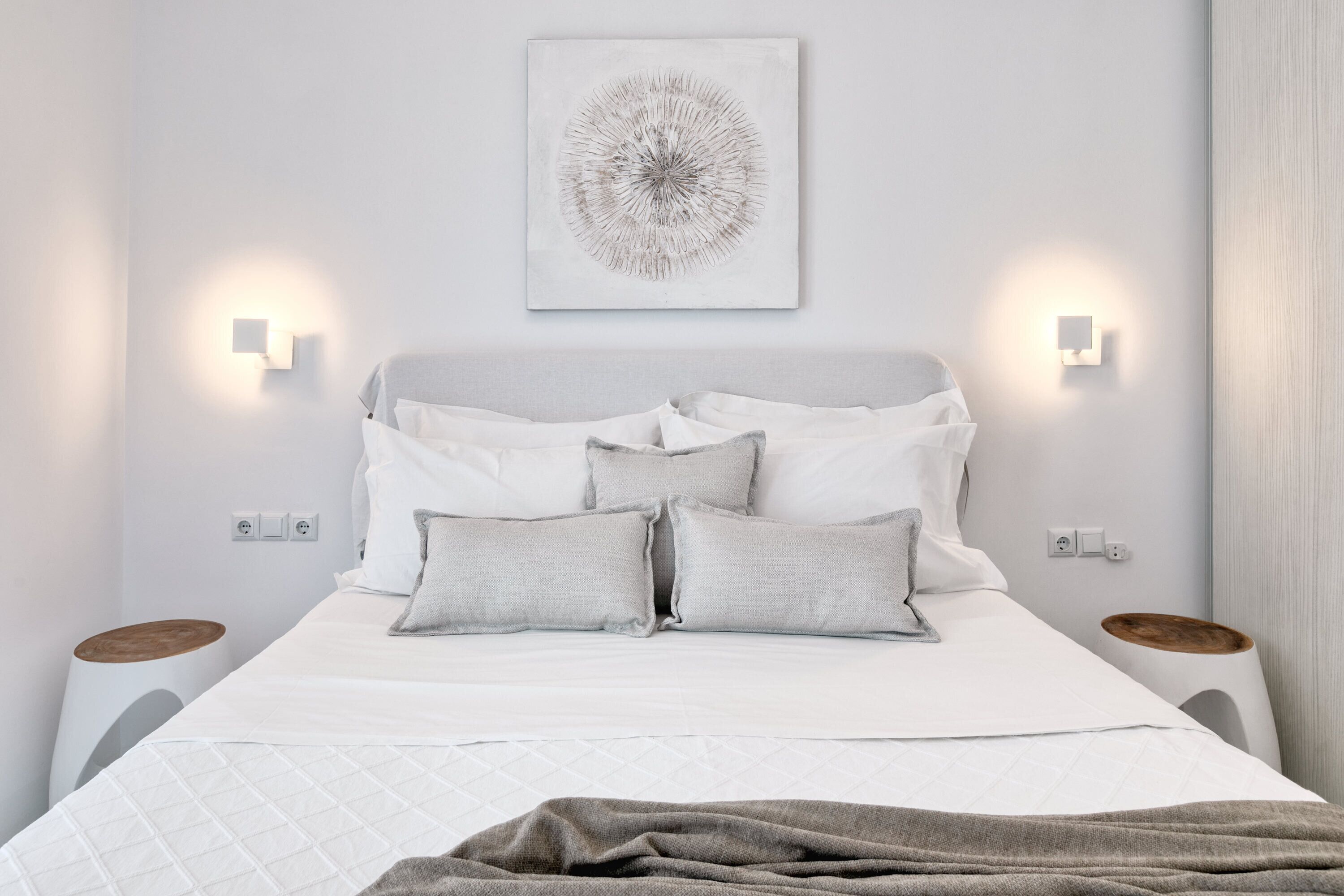 Quarto moderno com cama, duas mesas de cabeceira, arandela e uma obra de arte emoldurada.