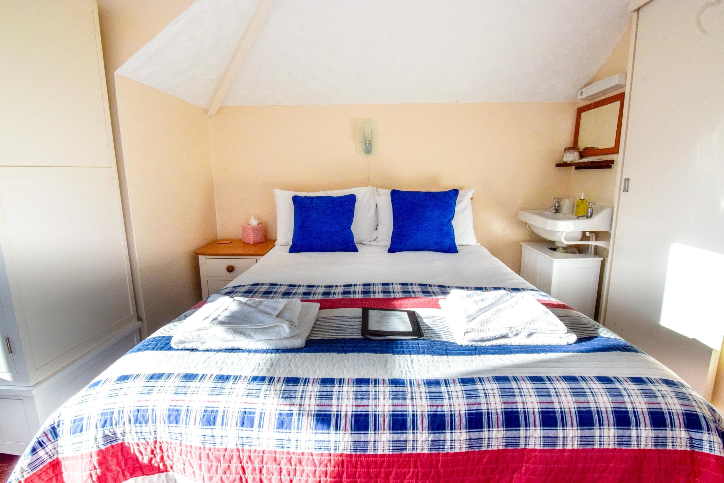 Quarto com cama, mesa de cabeceira, espelho e banheiro com pia.