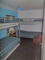 Quarto com beliche, parede azul, cadeira de madeira e luminária pendente.