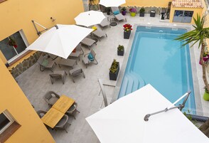 Área de piscina externa com espreguiçadeiras, guarda-sóis e plantas em vasos.