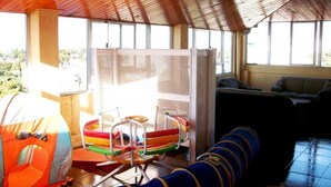 Quarto com teto de madeira alto, parede com janelas, área de brincar colorida e um sofá.