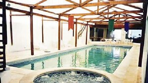 Uma área de piscina com hidromassagem, vigas de madeira e um espaço de estar coberto.
