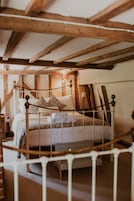 Quarto com teto de madeira, cama com roupa de cama branca e luminária na parede.
