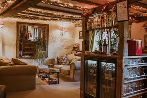 Uma sala de estar acolhedora com um sofá, poltrona e mesa de centro. Há uma estante com vários objetos e uma pequena planta.