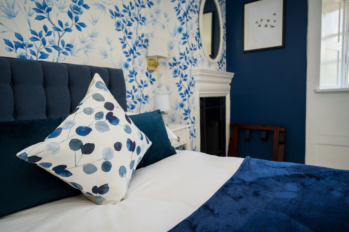 Quarto com cama, almofadas, mesa de cabeceira, espelho e lareira.