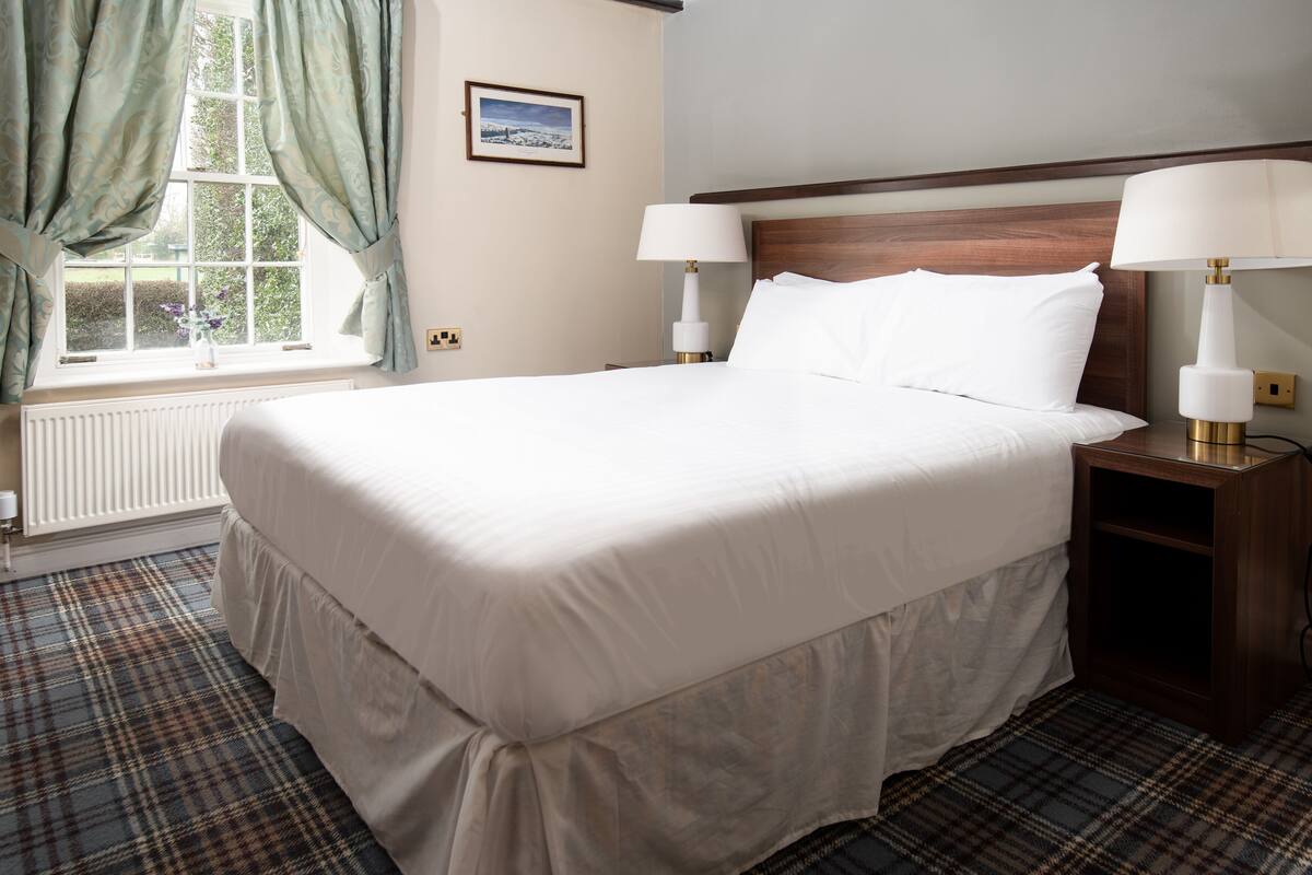 Cama bem arrumada com lençóis brancos, cabeceira de madeira e duas luminárias de cabeceira.