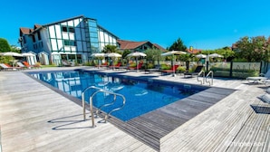 Piscina com espreguiçadeiras e guarda-sóis, cercada por um deck de madeira e um edifício com design moderno.