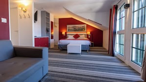 Quarto de hotel com cama, sofá, escrivaninha e uma janela grande.