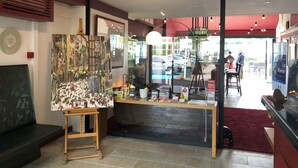 Interior de café com balcão de madeira, uma pintura grande e tapete vermelho.
