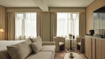 Quarto de hotel com cama, sofá, mesa pequena com uma xícara, máquina de café e televisão.