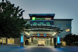 Entrada de um hotel Holiday Inn Express com galeria coberta e um banco em frente.