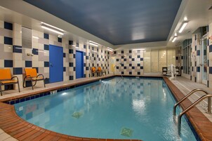 Piscina interna com paredes quadriculadas, uma porta azul e cadeiras laranja.