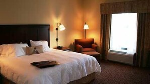 Quarto de hotel com uma cama grande, duas luminárias de cabeceira, uma cadeira e uma janela com cortinas.