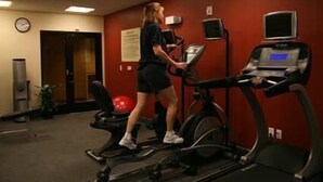 Uma academia com esteiras, uma parede vermelha, um relógio e uma porta.