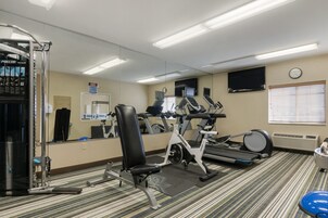 Uma academia com equipamentos de exercício, um espelho, um relógio e uma televisão na parede.