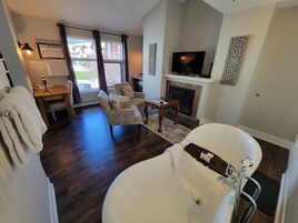 Uma sala de estar moderna com uma banheira grande e branca, uma lareira, uma televisão e uma área de jantar com mesa e cadeiras.