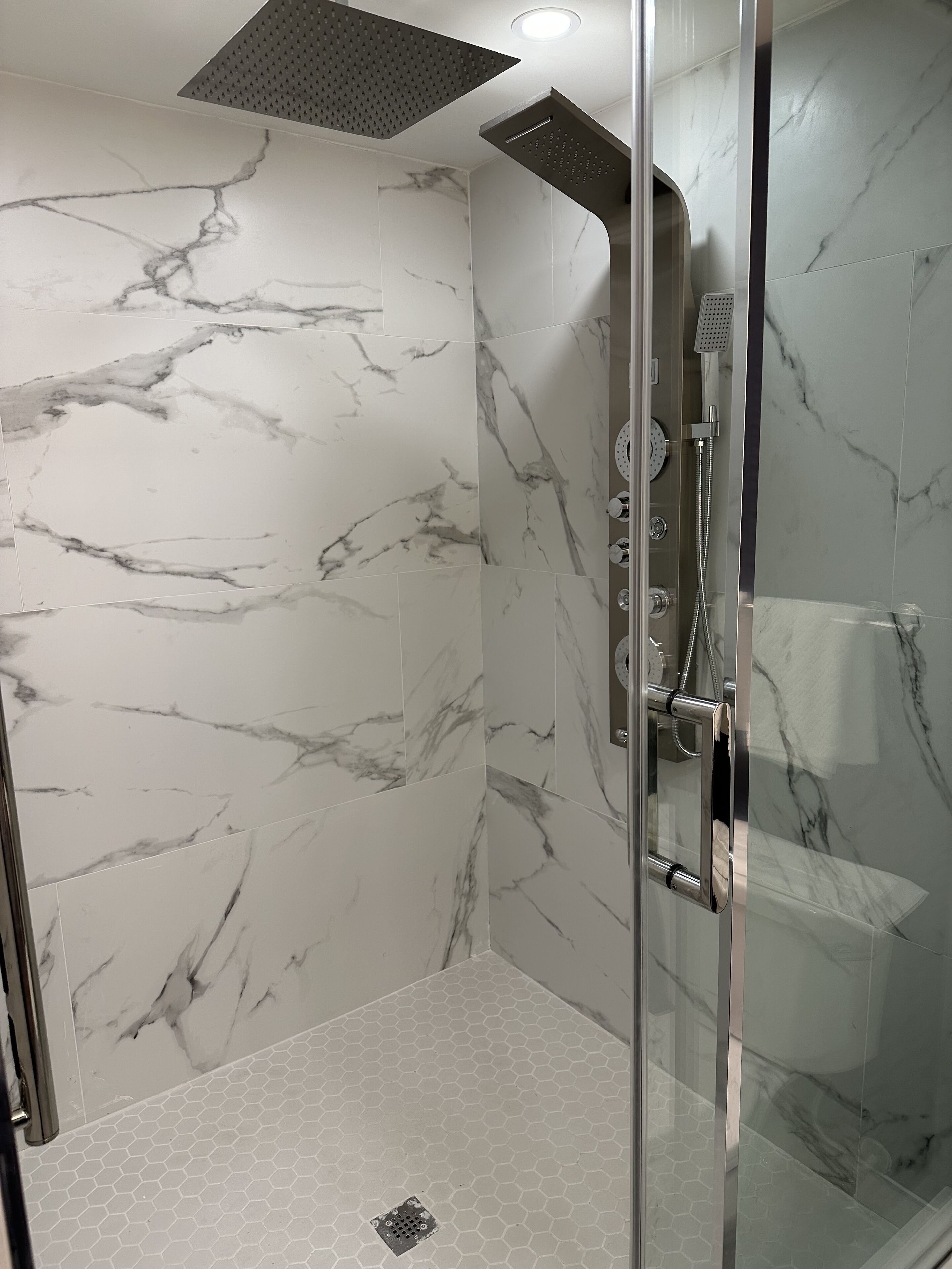 Um chuveiro moderno com porta de vidro, paredes de mármore e chão de azulejos hexagonais.