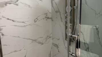 Um chuveiro moderno com porta de vidro, paredes de mármore e chão de azulejos hexagonais.
