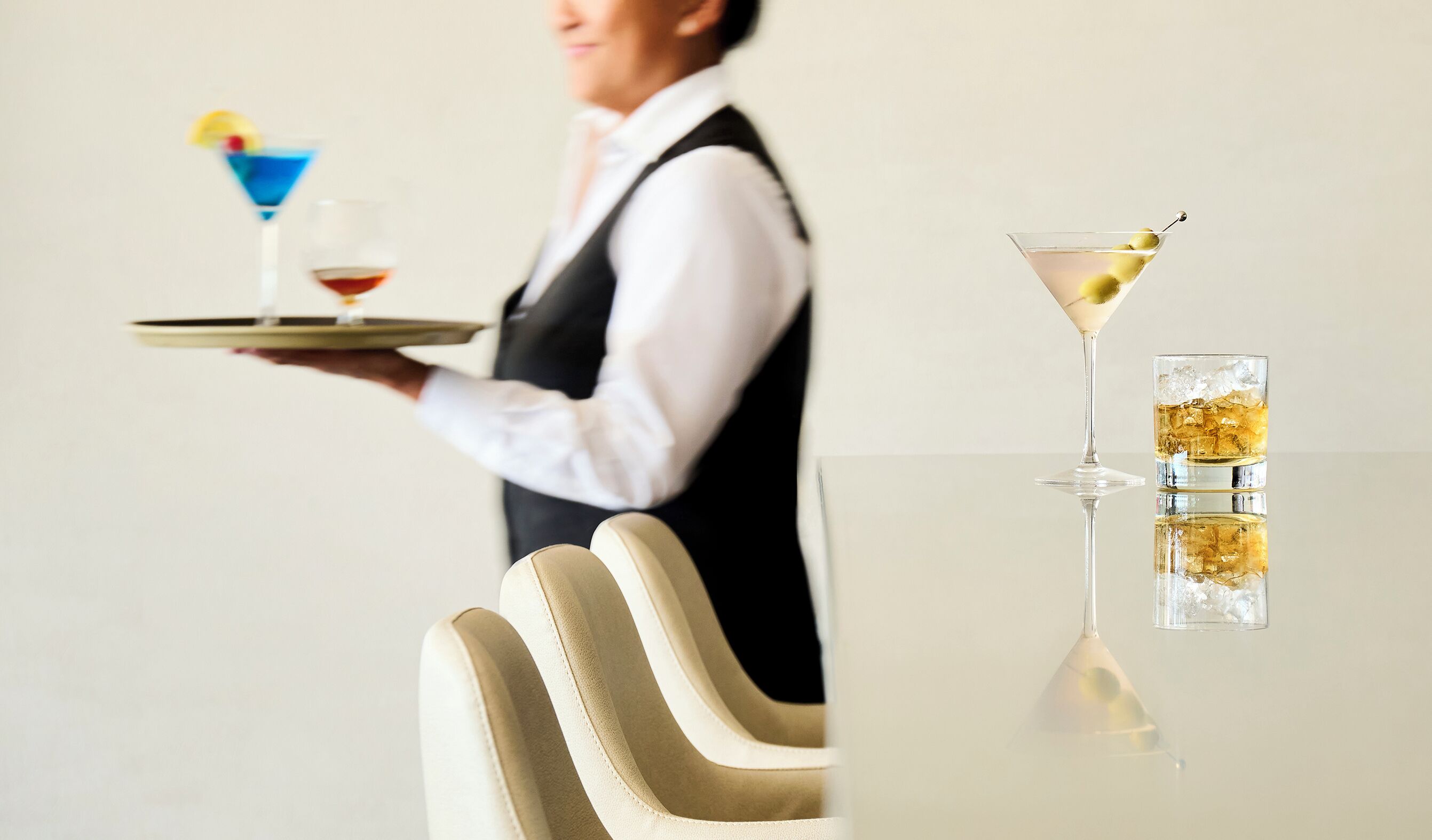 Garçom carregando uma bandeja com um copo de martini e um copo de vinho.