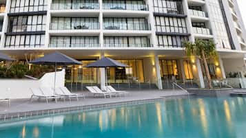 Um hotel moderno com área de piscina, espreguiçadeiras e guarda-sóis.