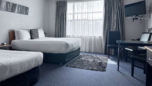 Quarto de hotel com duas camas, uma escrivaninha com cadeira, televisão e uma janela grande com cortinas.