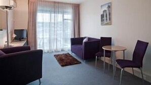 Quarto de hotel moderno com sofá, poltronas, uma mesinha e uma televisão.