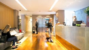 Um lobby moderno de hotel com balcão de recepção, um sofá e piso de madeira.