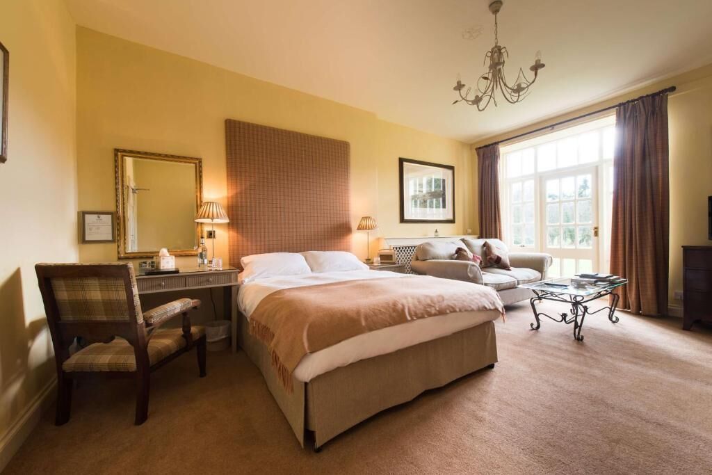 Quarto de hotel com uma cama grande, uma escrivaninha, uma cadeira, um sofá, uma mesa de centro e um candelabro.