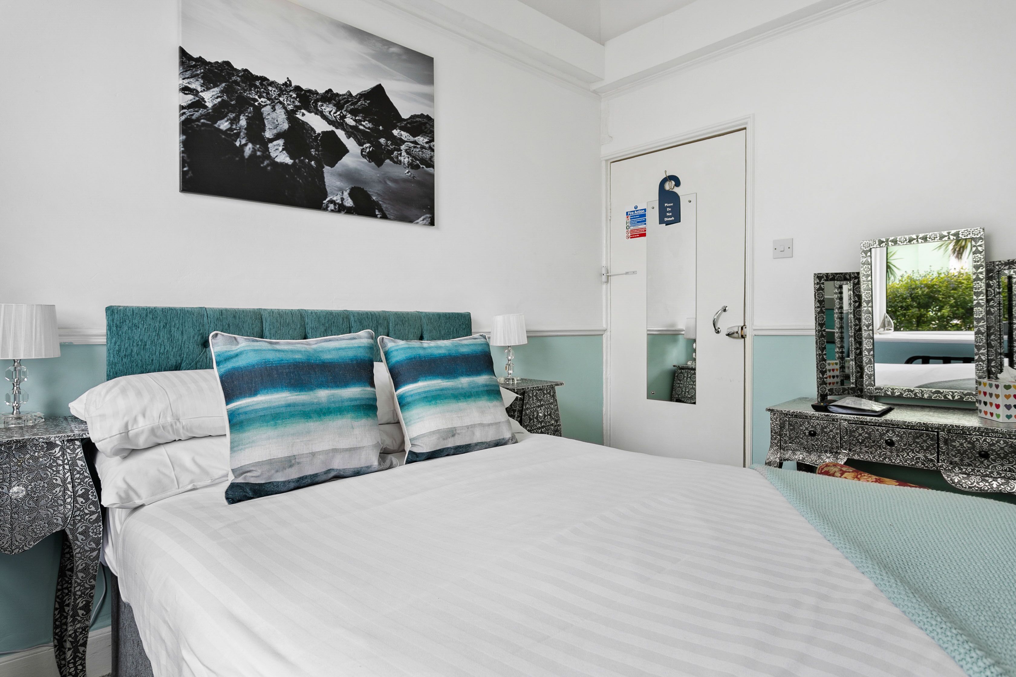 Quarto com cama, mesa de cabeceira, cômoda, espelho e porta.