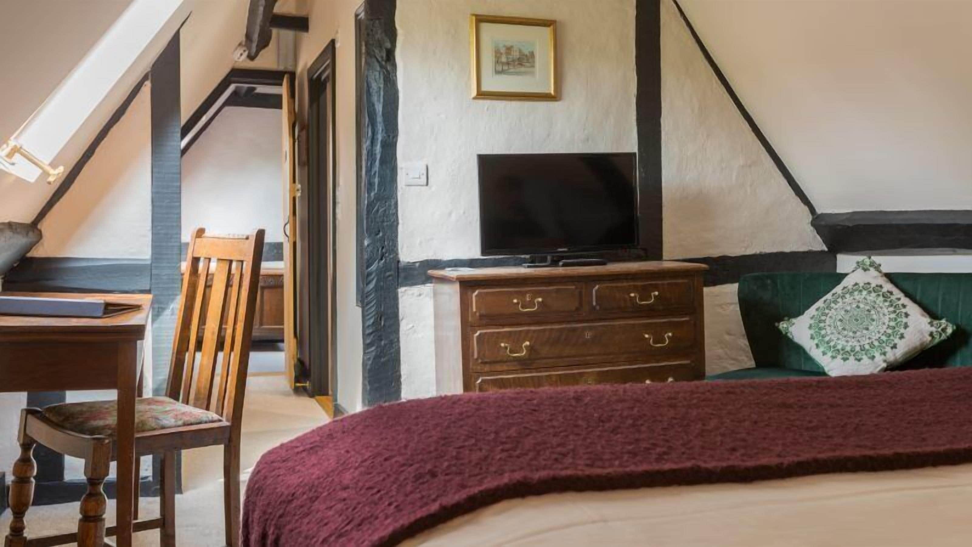 Um quarto com cama, cómoda de madeira, televisão, cadeira e escada que dá para um andar superior.