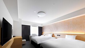 Quarto de hotel com duas camas, uma televisão, uma escrivaninha e uma janela grande.