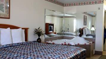 Quarto de hotel com uma cama, um espelho grande, uma televisão e uma pequena mesa com abajur.