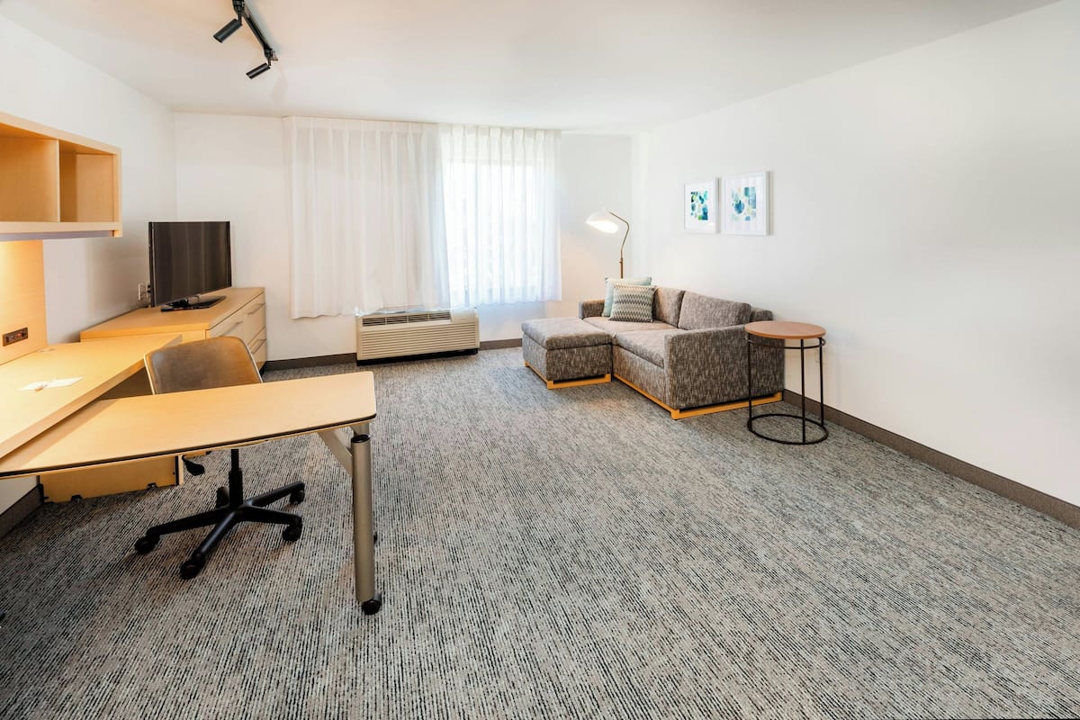 Quarto de hotel moderno com uma escrivaninha, um sofá, uma mesinha e um abajur.