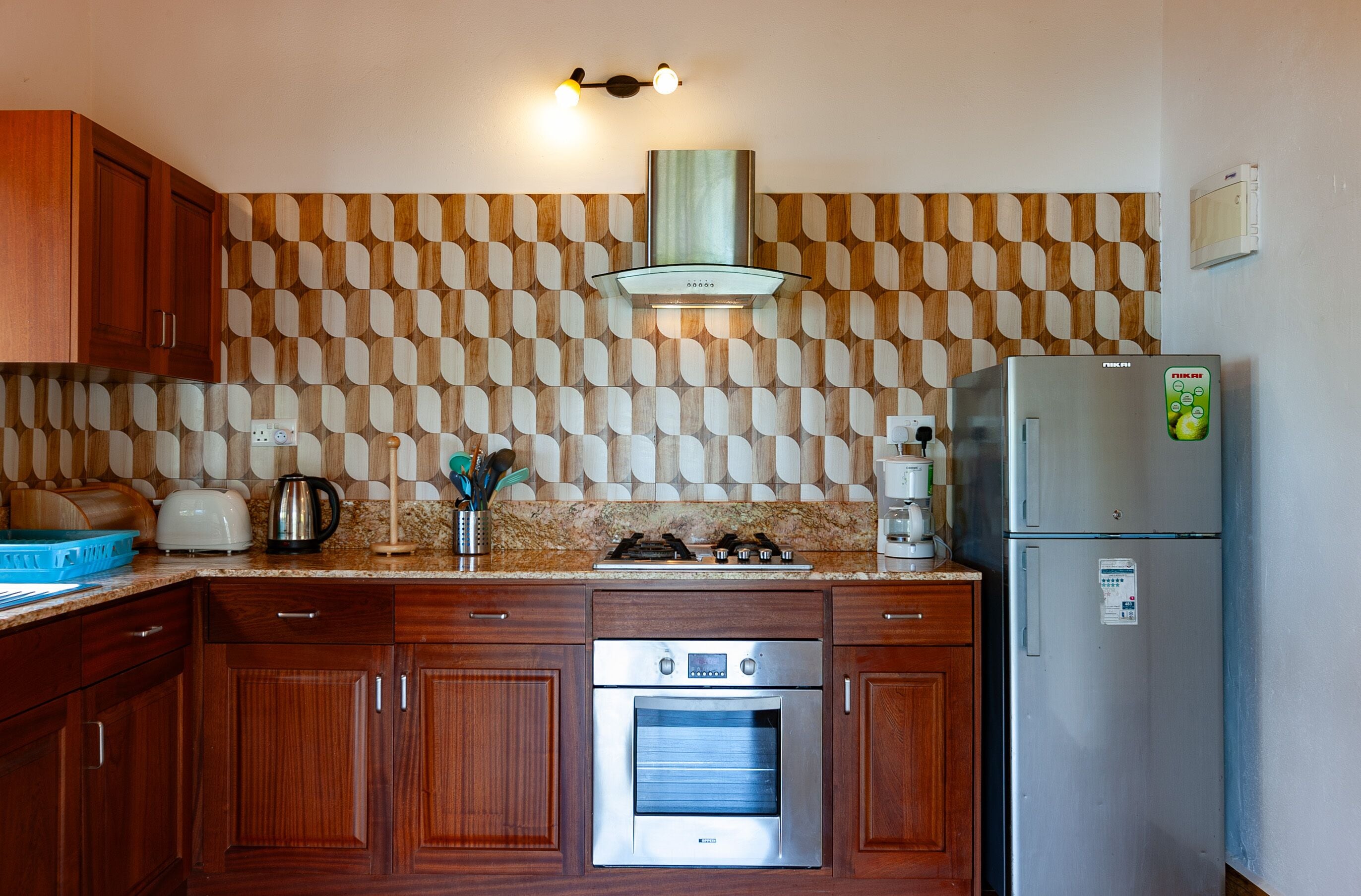 Uma cozinha com armários de madeira, forno embutido, geladeira de aço inoxidável e painel de fundo padronizado.