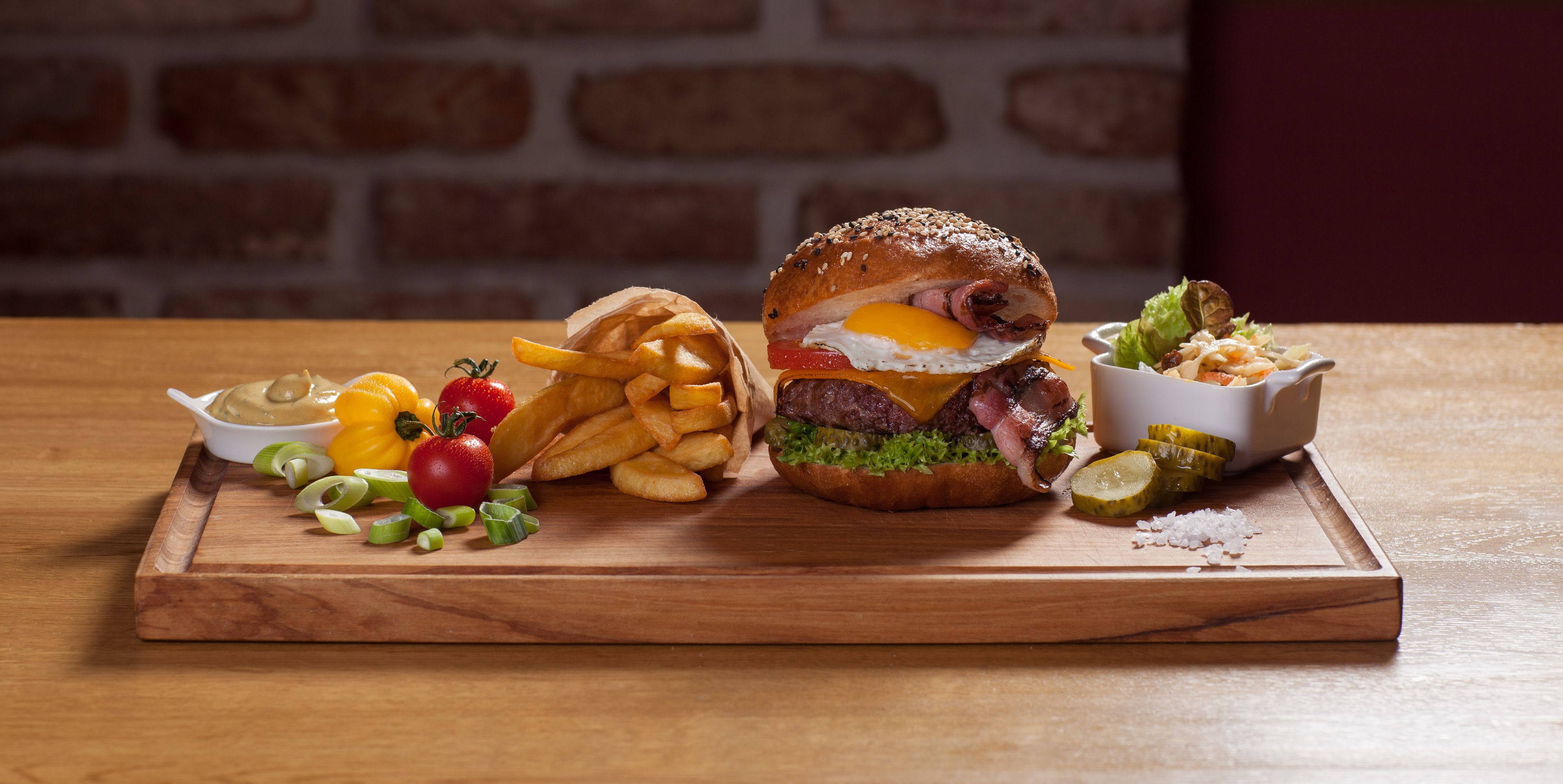 Uma mesa de madeira com um hambúrguer, batatas fritas e uma salada.