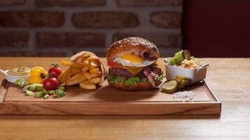 Uma mesa de madeira com um hambúrguer, batatas fritas e uma salada.