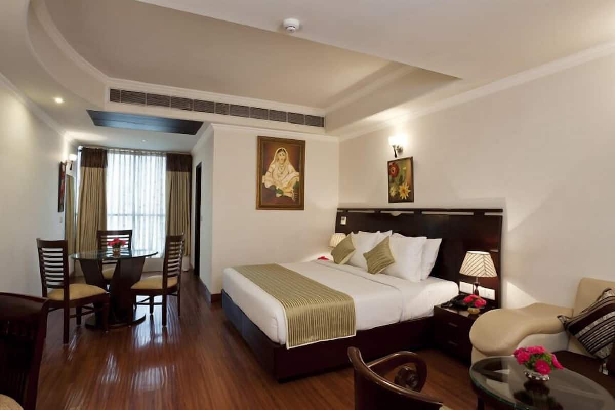Quarto de hotel com uma cama grande, uma escrivaninha com cadeira, uma mesinha com um vaso e um sofá.
