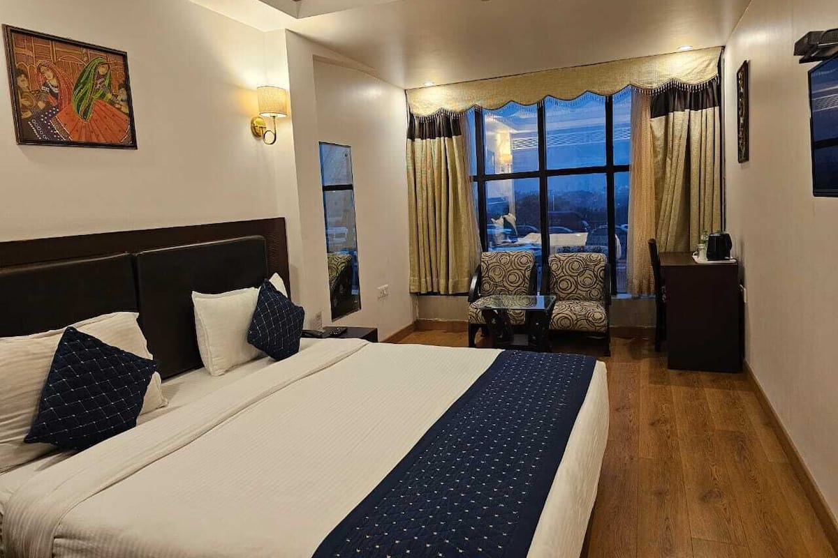 Quarto de hotel com uma cama grande, uma escrivaninha, uma cadeira e vista da cidade por grandes janelas.
