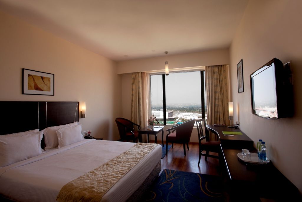 Quarto de hotel com uma cama grande, uma escrivaninha, uma cadeira, televisão e janela com vista.