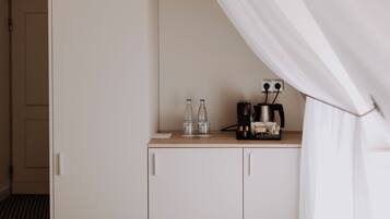 Quarto de hotel com minibar, duas garrafas de água, máquina de café e tomada.