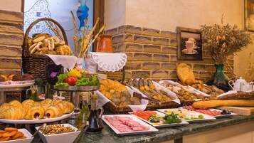 Um buffet com diversos pães, doces e carnes.