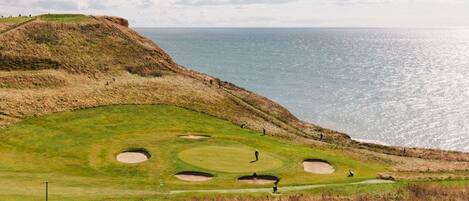 Um campo de golfe costeiro com bunkers e vista para o mar.