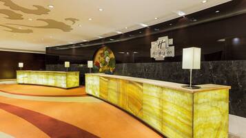 Uma área de recepção de hotel com balcões de mármore, uma grande obra de arte floral e uma placa com a inscrição 'Holiday Inn'.