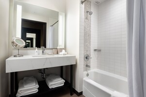 Uma casa de banho moderna com uma toucador branco, um espelho grande, uma banheira e um chuveiro com porta de vidro.