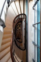 Uma escadaria em espiral com corrimão de metal, degraus bege e parede estampada.