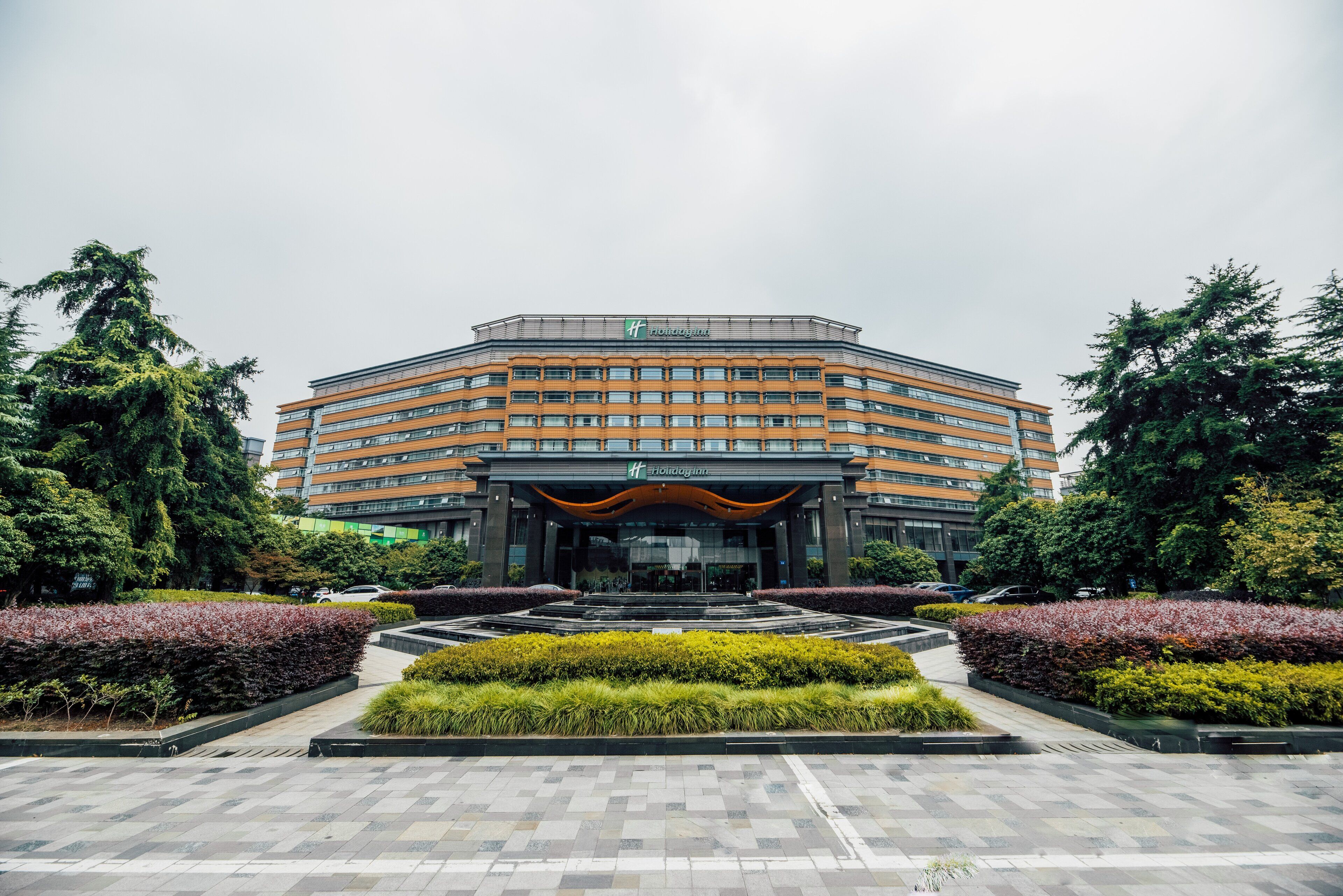 Um hotel moderno com fachada curva, entrada central e jardins ajardinados.