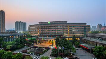 Um hotel Holiday Inn com design moderno, apresentando um pátio central com uma fonte, cercado por vegetação exuberante e vários espaços de estacionamento.