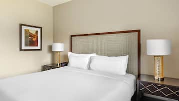 Quarto de hotel com uma cama grande, duas mesas de cabeceira com luminárias, uma imagem emoldurada na parede e uma cabeceira texturizada.